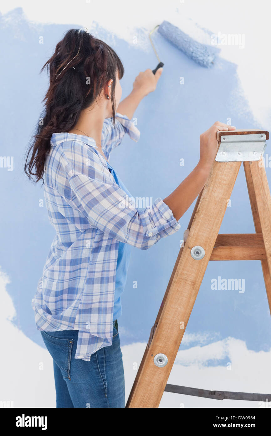 Woman using paint roller to paint wall blue Stock Photo - Alamy