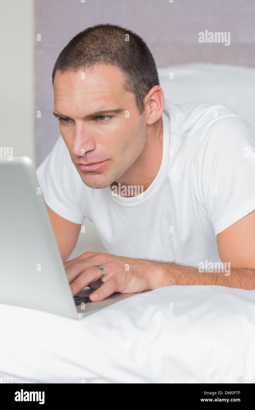 Serious man lying on bed using his laptop Stock Photo - Alamy