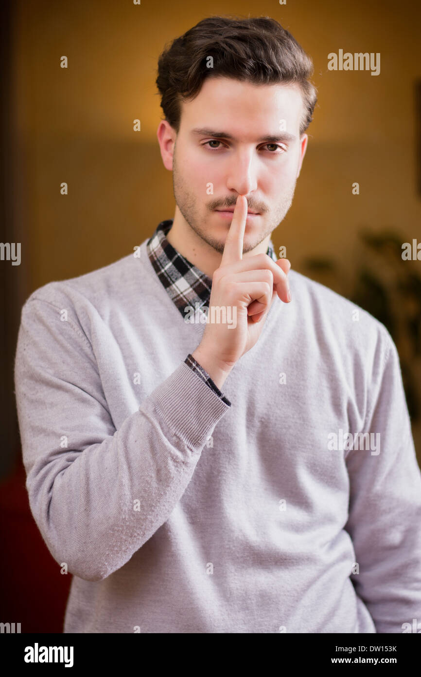 Handsome young man doing Hush sign with finger on lips, looking at ...