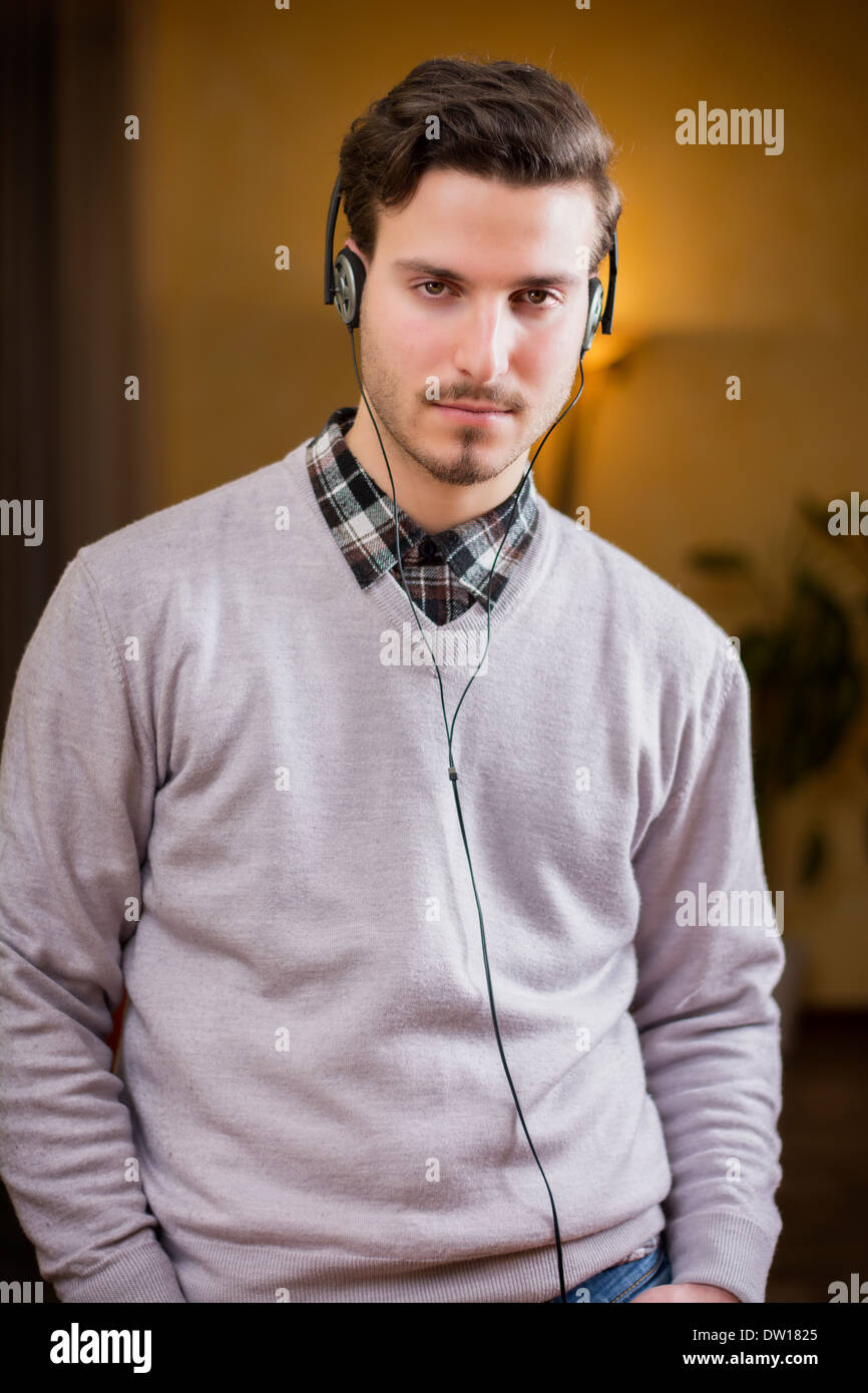 Attractive young man listening to music on headphones at home, looking at camera, serious Stock ...