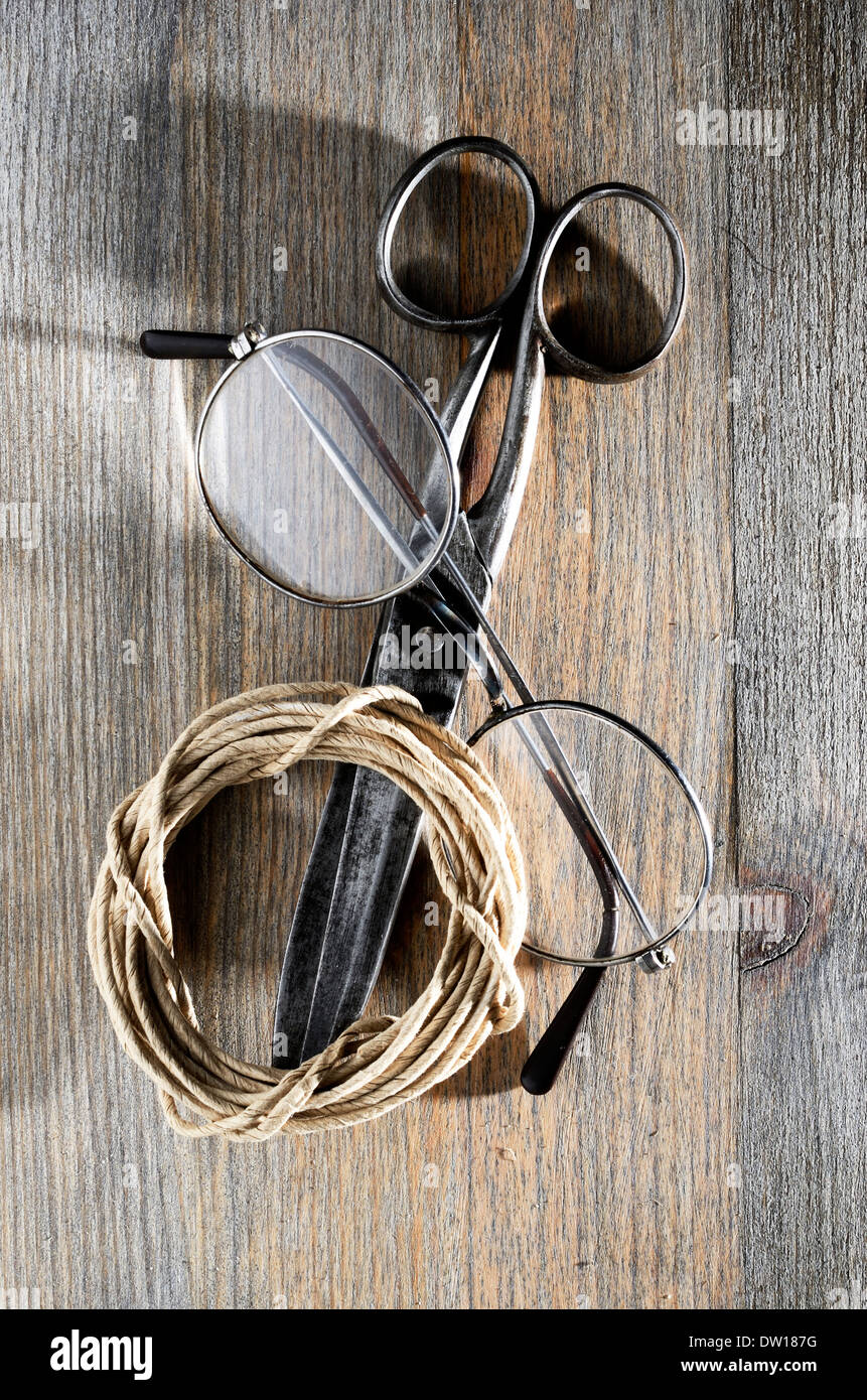 old scissors, glasses and hank of packthread over wooden background ...