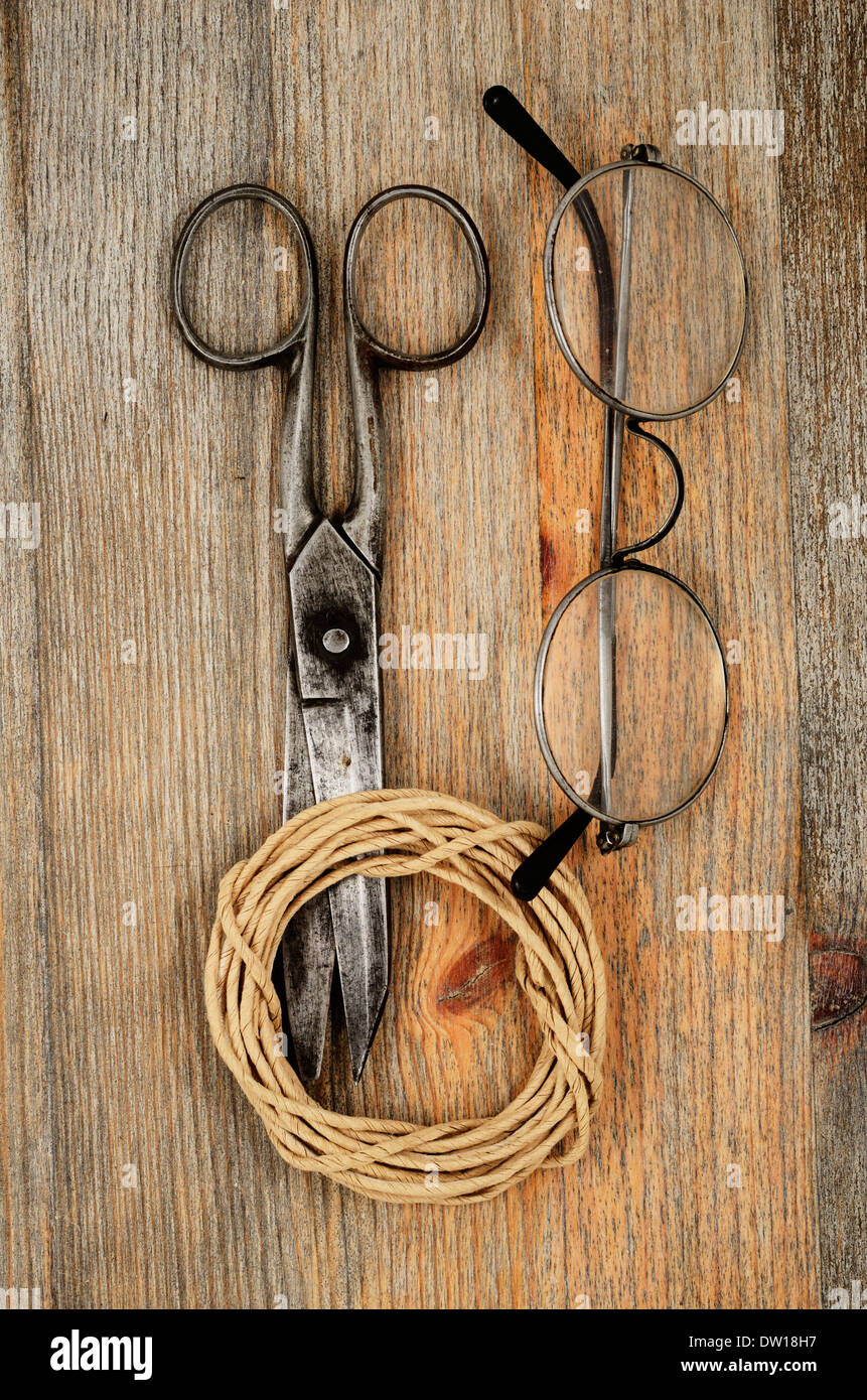 old scissors, glasses and hank of packthread over wooden background ...