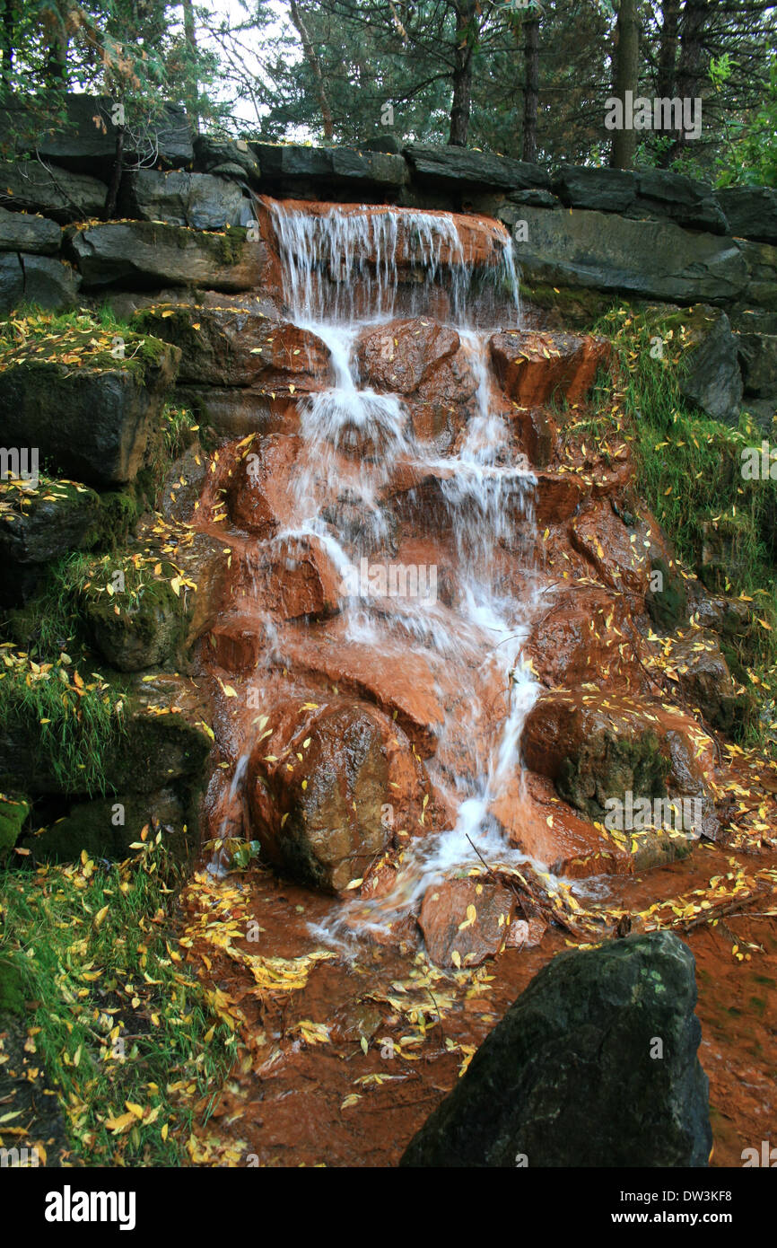 Small waterfall on rusty orange rocks with fallen yellow leaves ...
