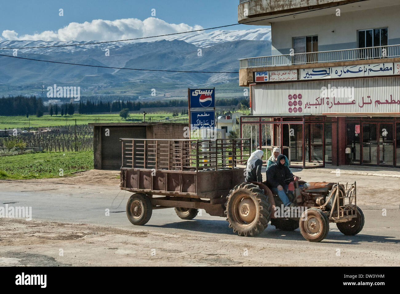 Three people riding on an ancient tractor pulling a wagon in the Bekaa ...