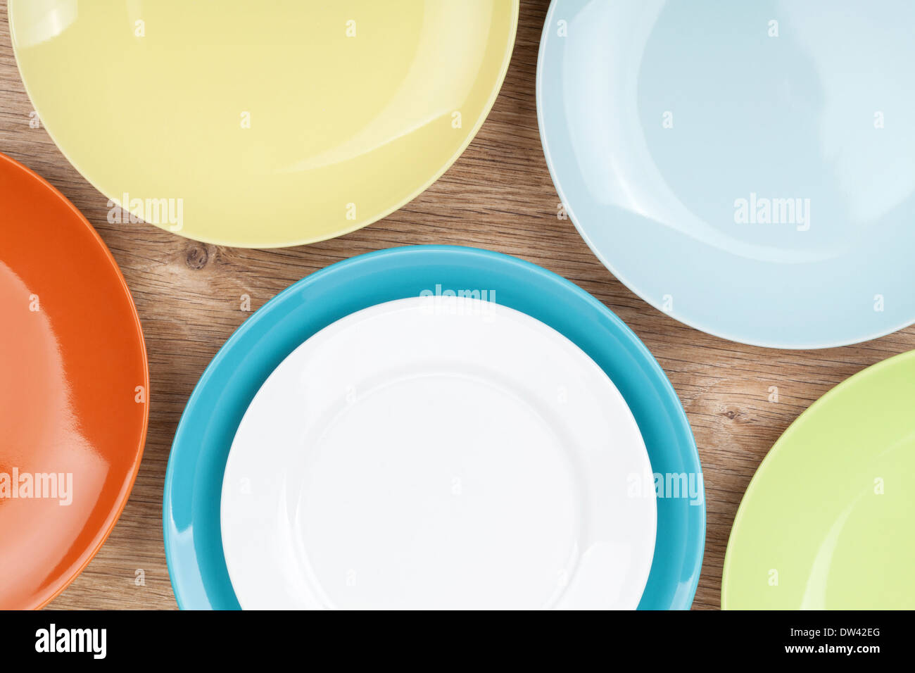 Colorful plates and saucers over wooden table background. View from ...