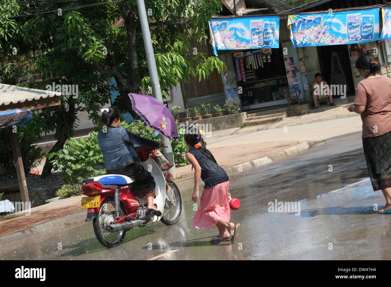 A young girl is throwing water at a woman riding a motorcycle during a ...