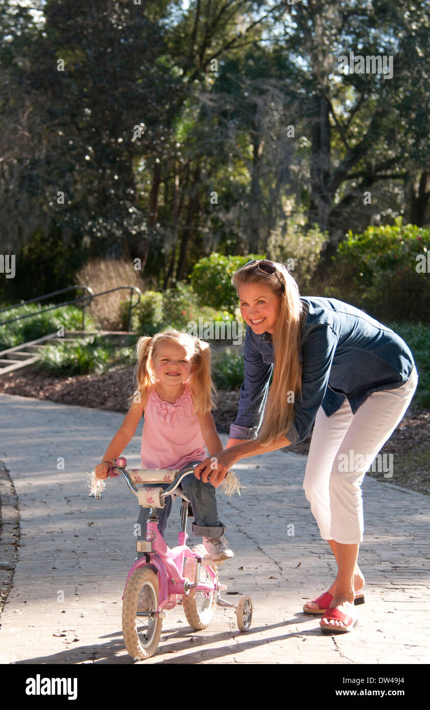 beautiful young mother and daughter riding bike and having fun outside ...