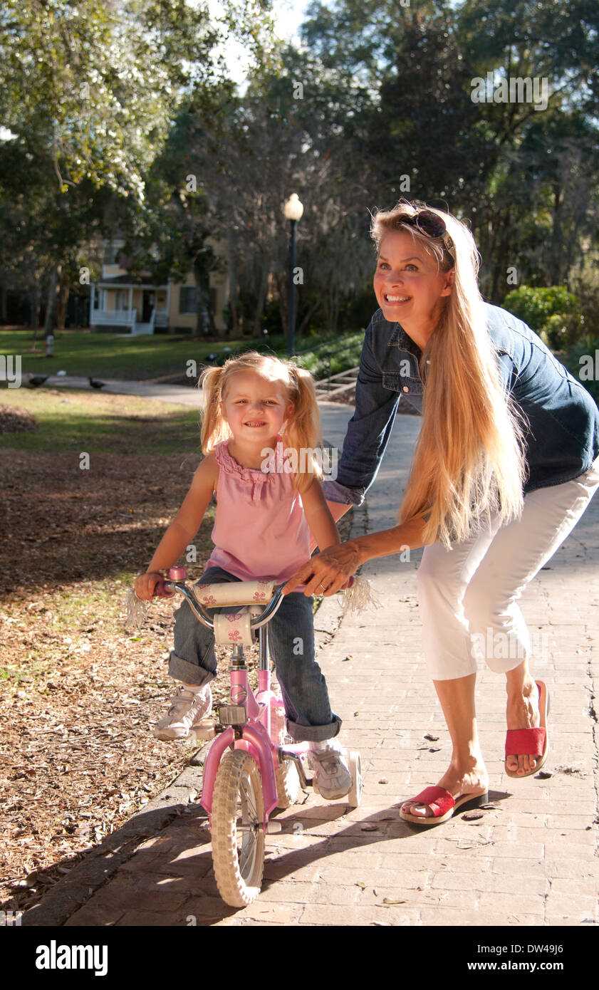beautiful young mother and daughter riding bike and having fun outside ...
