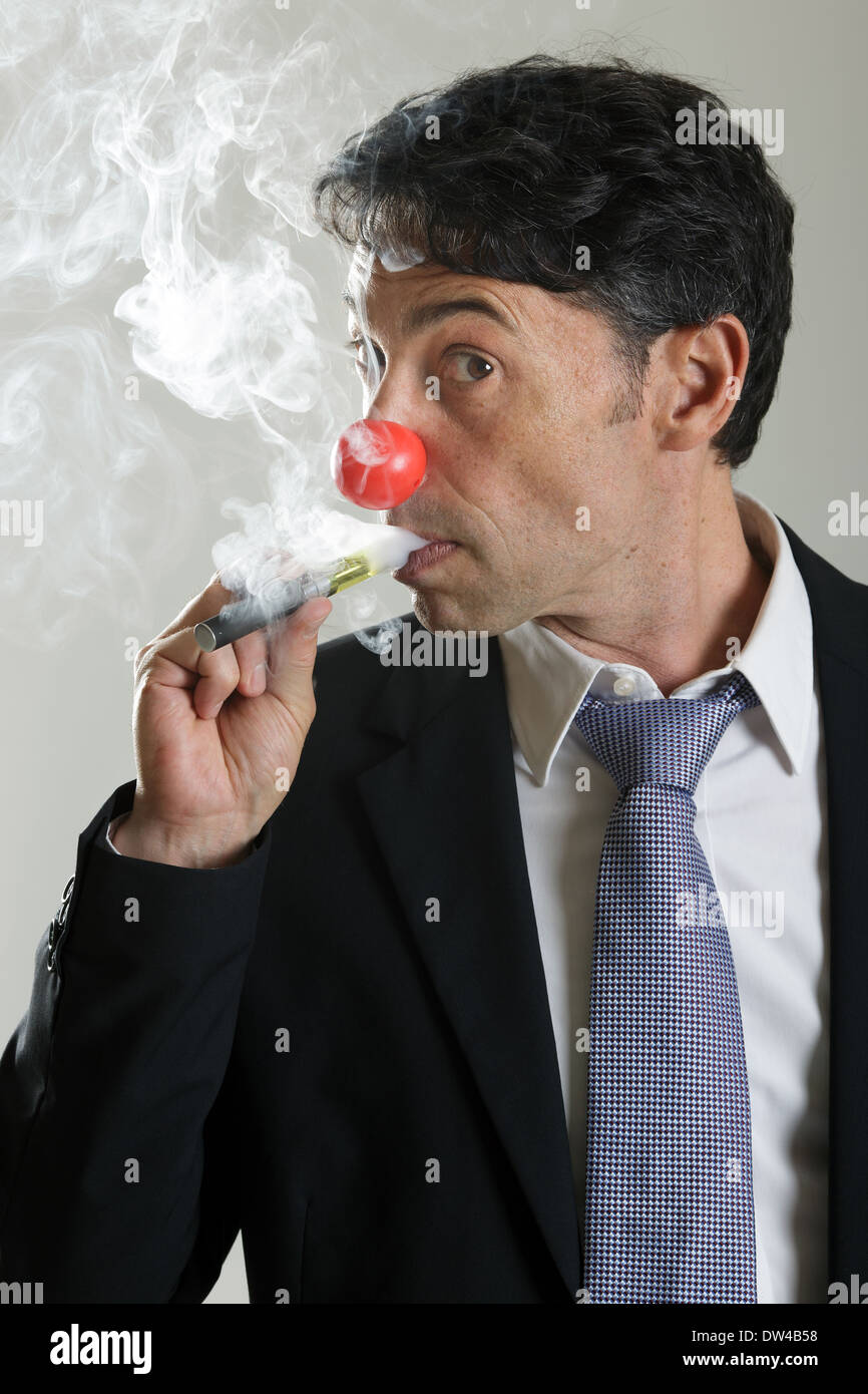 Middle-aged businessman wearing a red nose like a clown puffing on an e ...