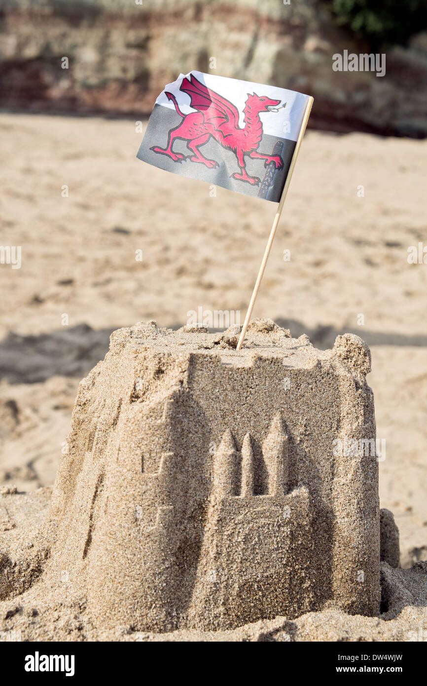 A sand castle on a sandy beach topped with the Welsh national flag ...