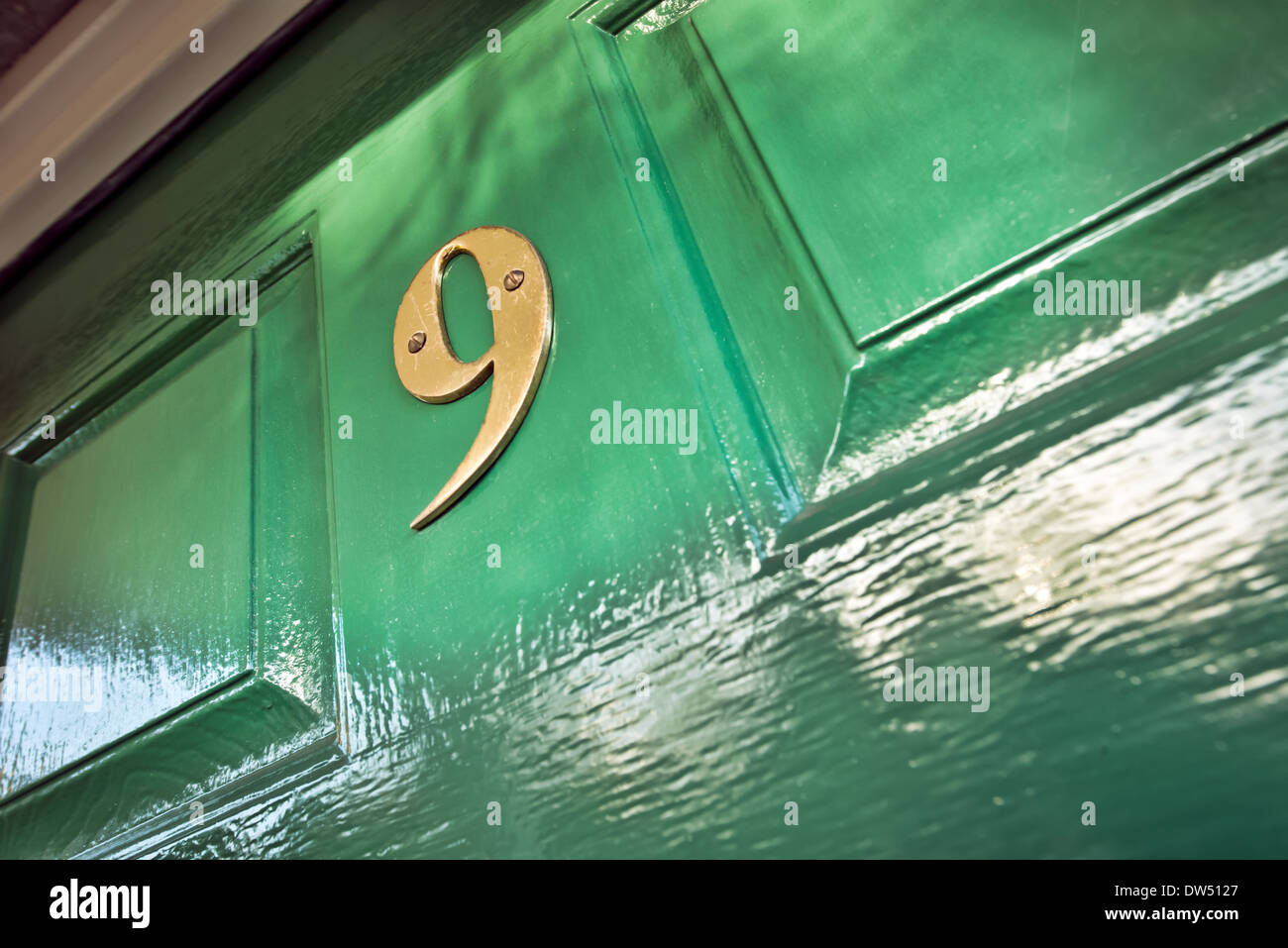 A brass number nine screwed to a green door Stock Photo - Alamy