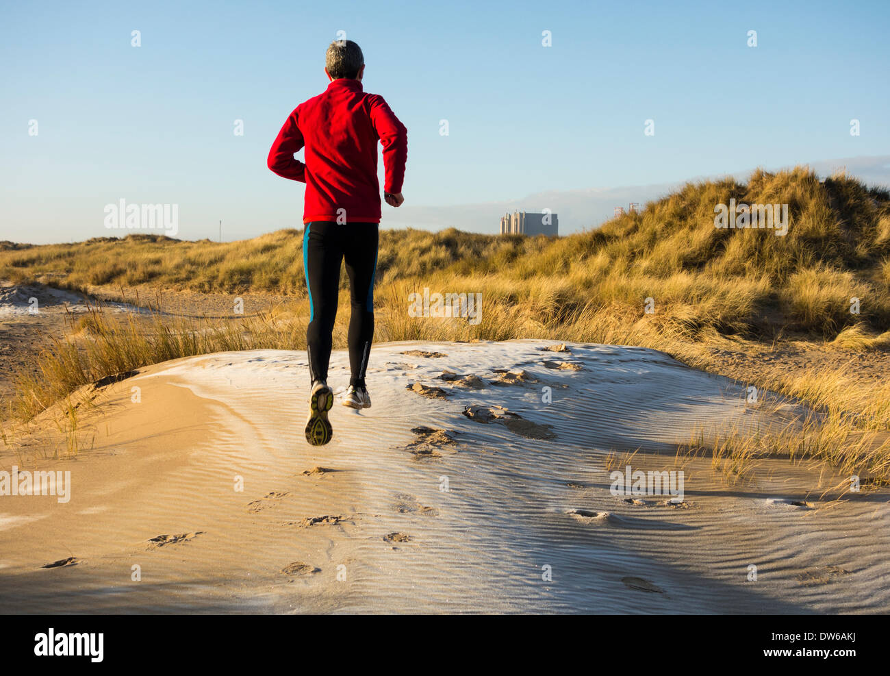 Mature man running on sand dunes covered in frost at Seaton Carew on ...