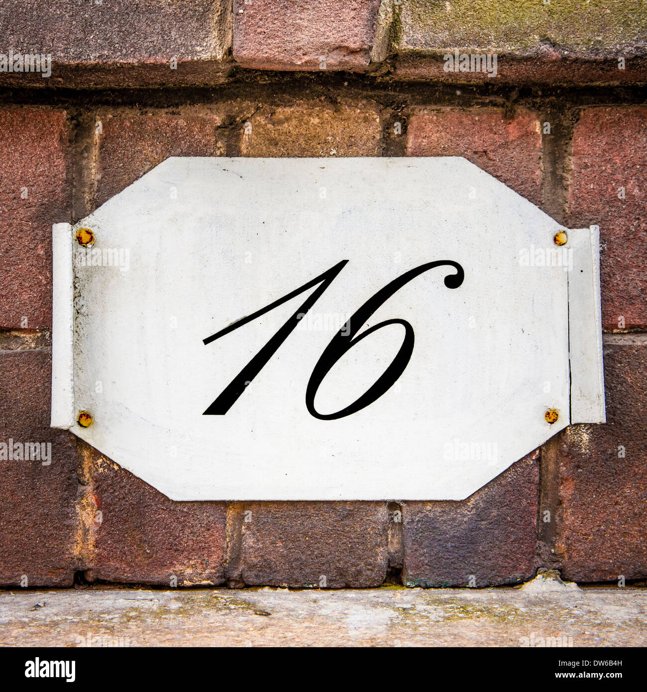 house number sixteen on a plate with curled edges, attached to a brick ...