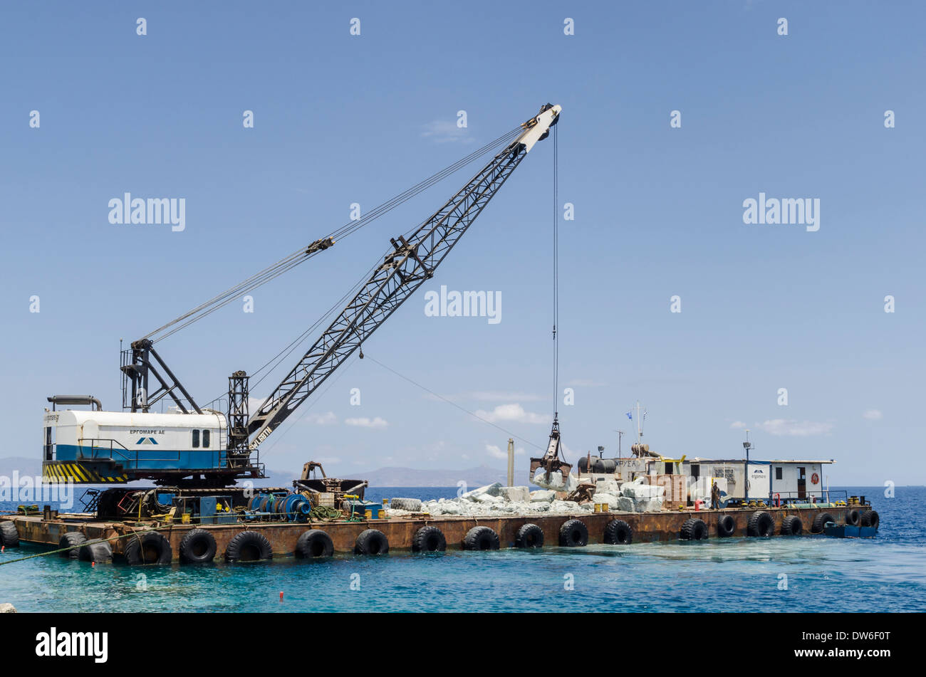 Barge with crane lifting rocks for a sea wall along the outer harbour ...