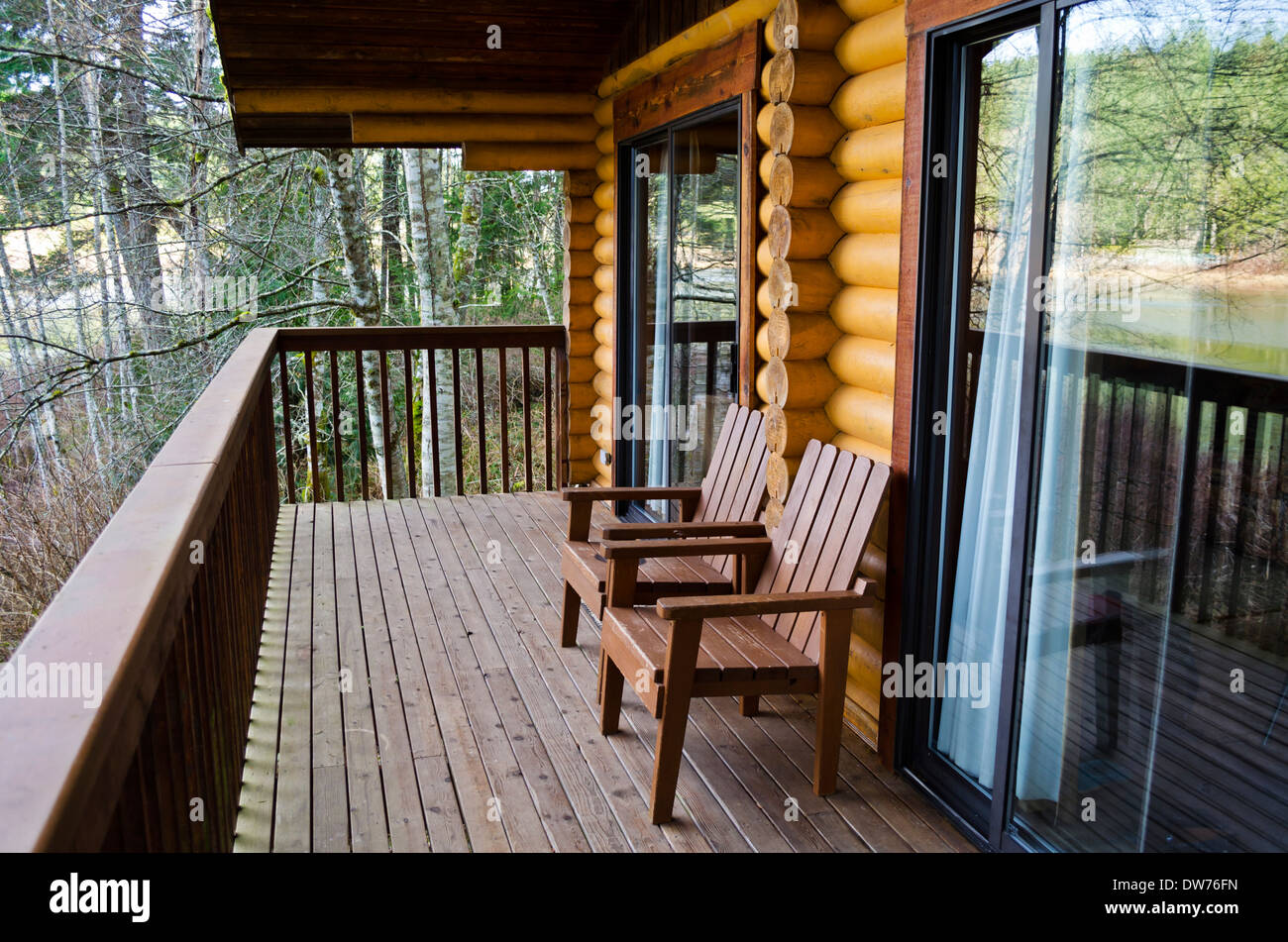 Log cabin deck with two wooden chairs facing the lake by the forest. At ...