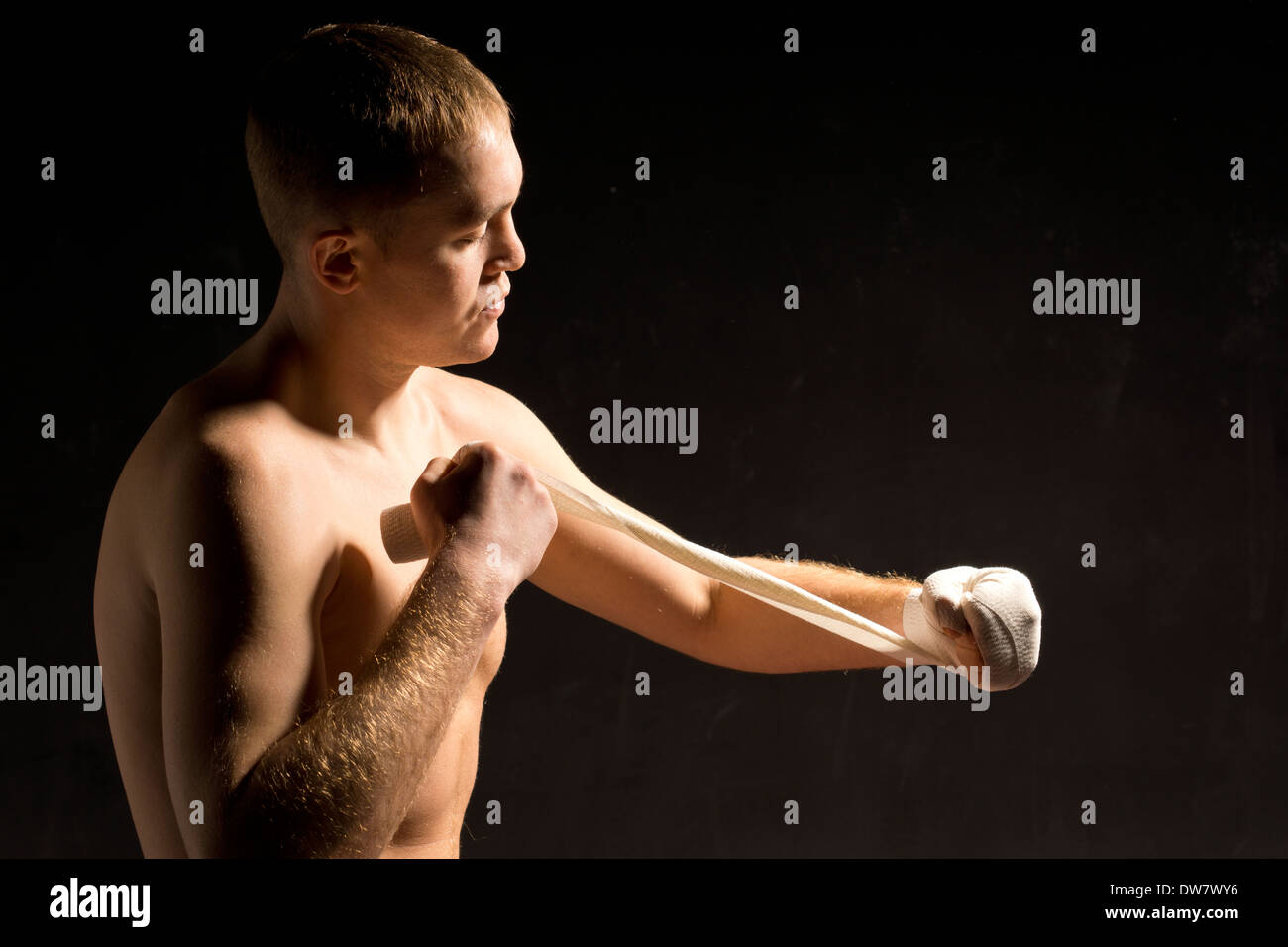 Dark dramatic image of a barechested young boxer putting on his ...