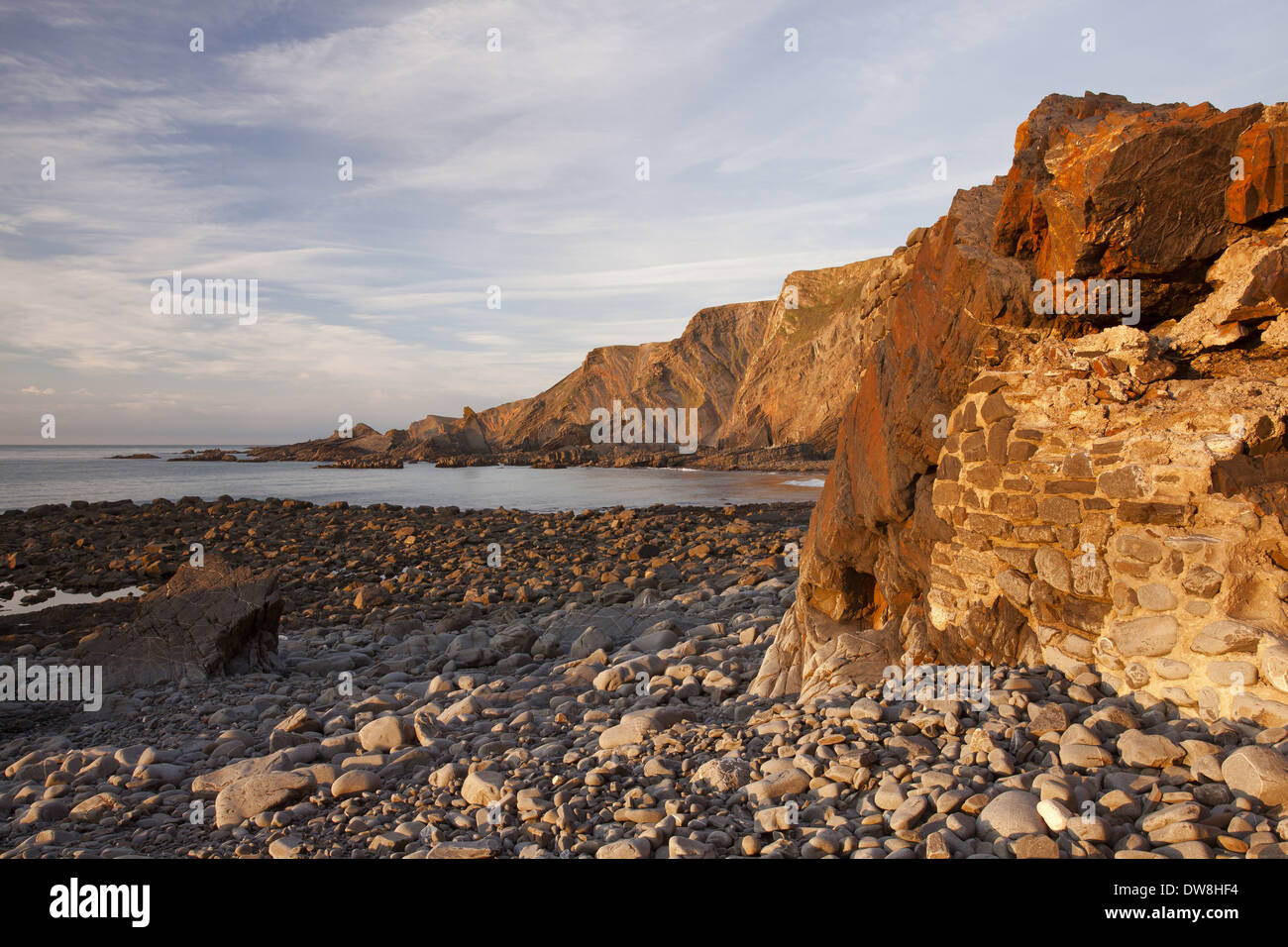 Manmade seawall and coastal cliff with folded strata at sunset Warren ...