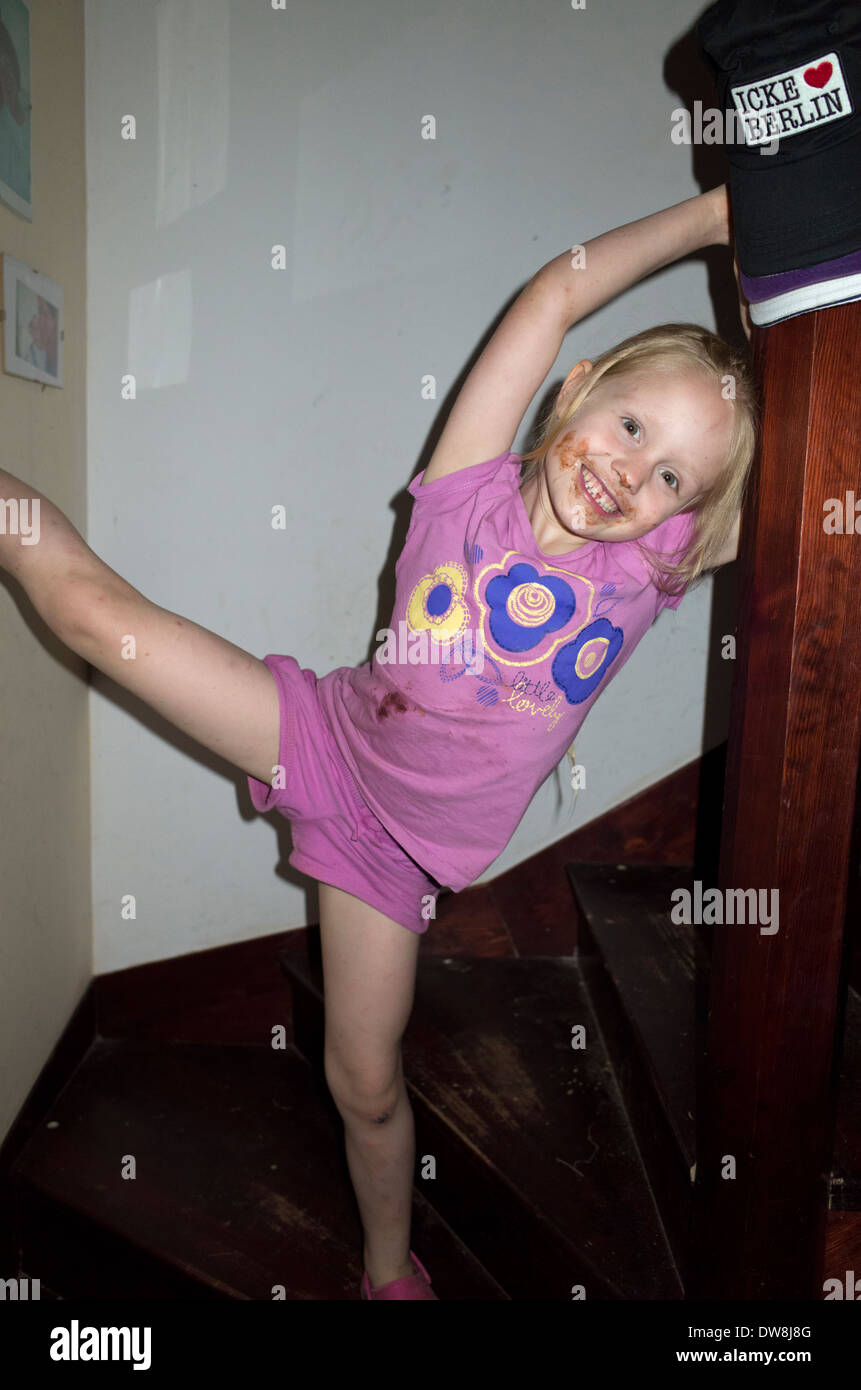 Happy girl age 6 standing on one leg with chocolate dessert on her face ...