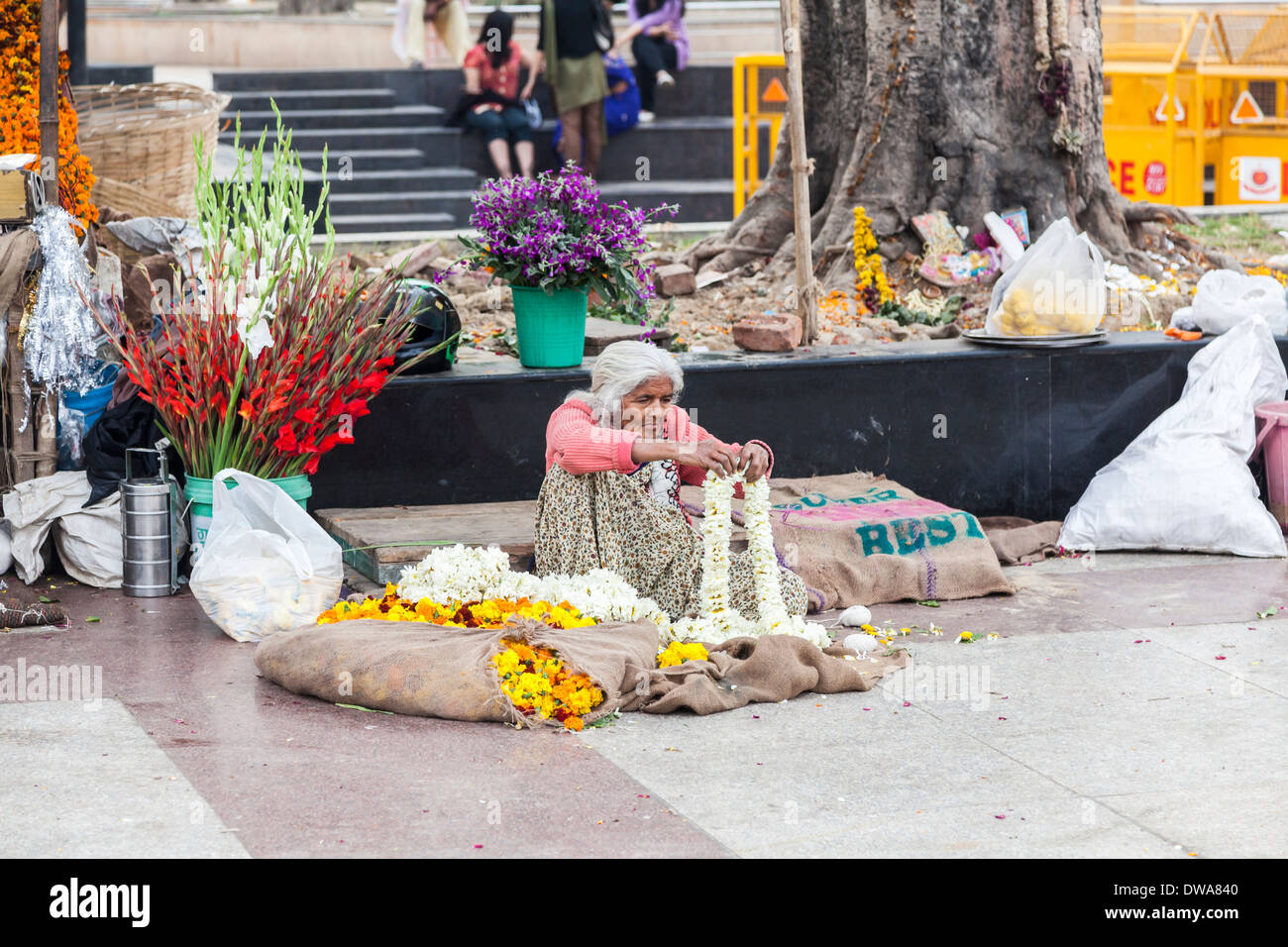 Old Indian woman at a flower stall sitting on the pavement making ...