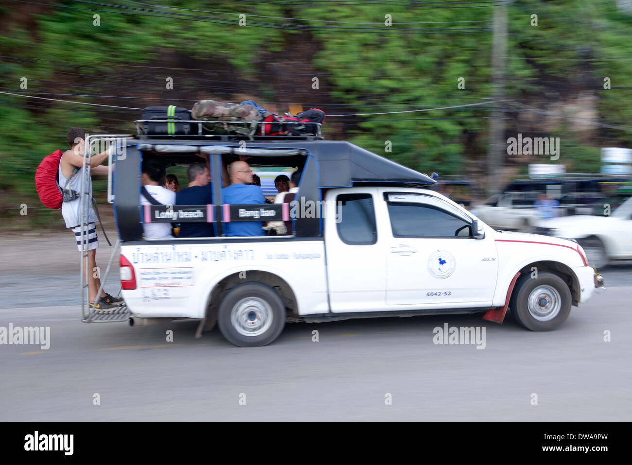Tourists riding on the bumper of a crowded shared taxi, also known as a ...