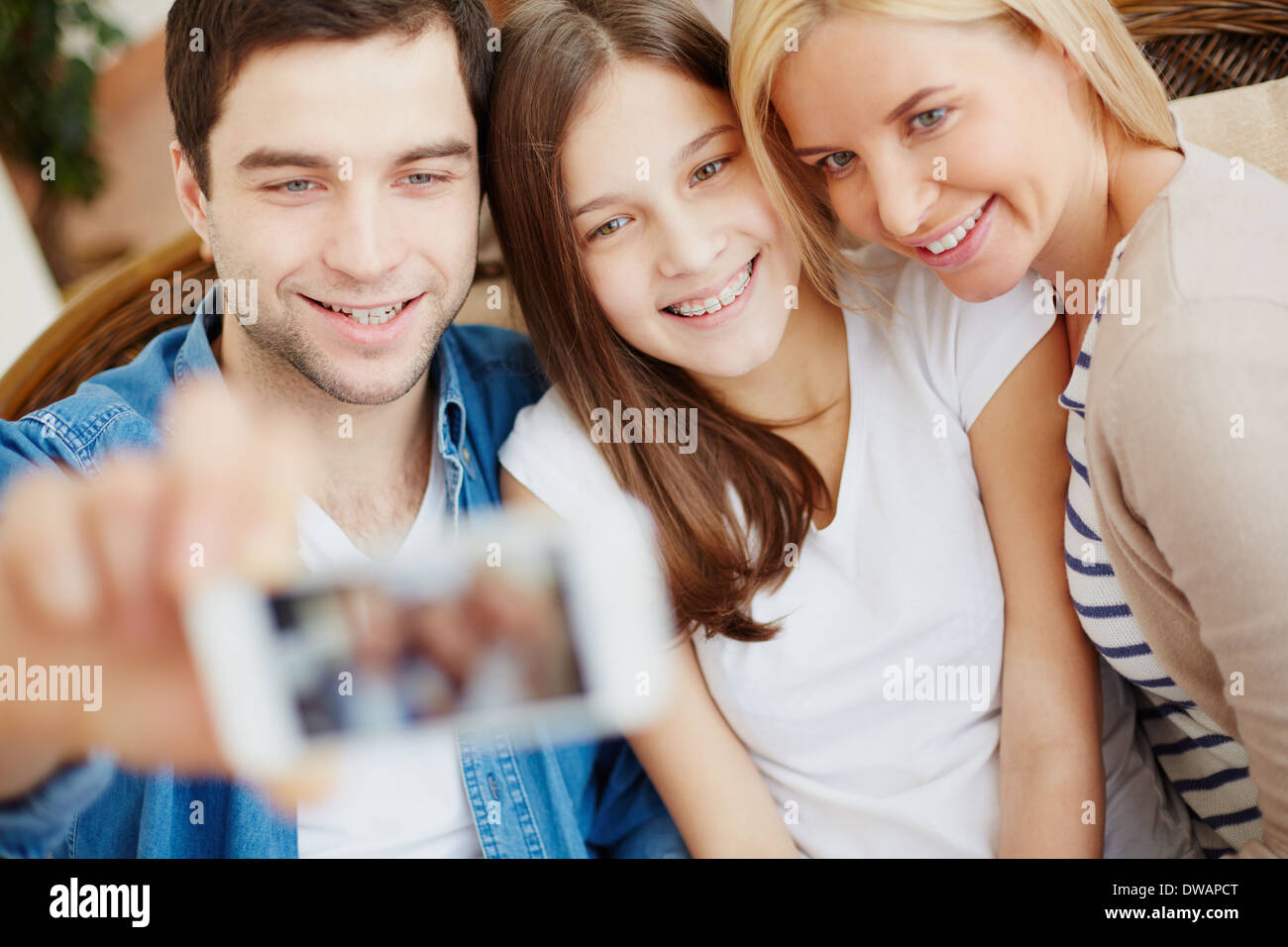 Young man holding cellular phone with happy daughter and wife near by ...