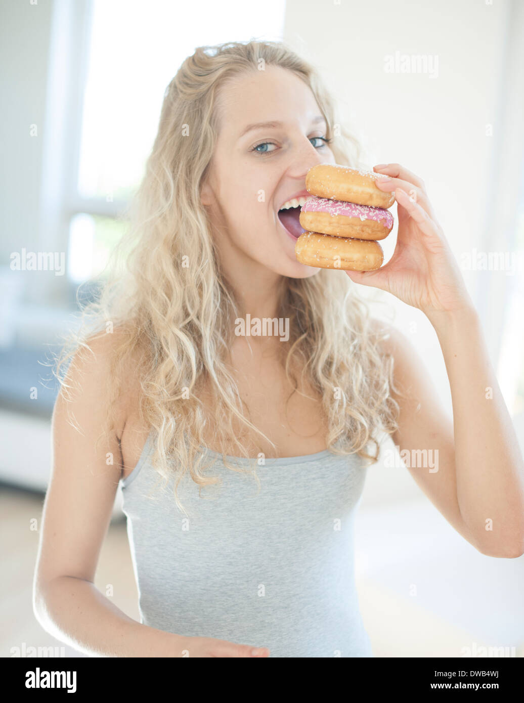 Portrait of happy woman eating donuts in house Stock Photo - Alamy