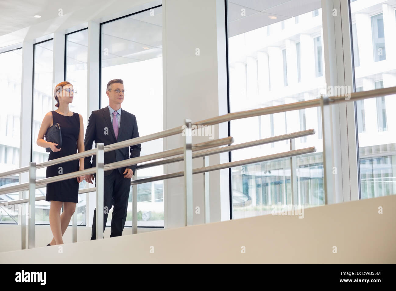 Business people walking by railing in office Stock Photo - Alamy