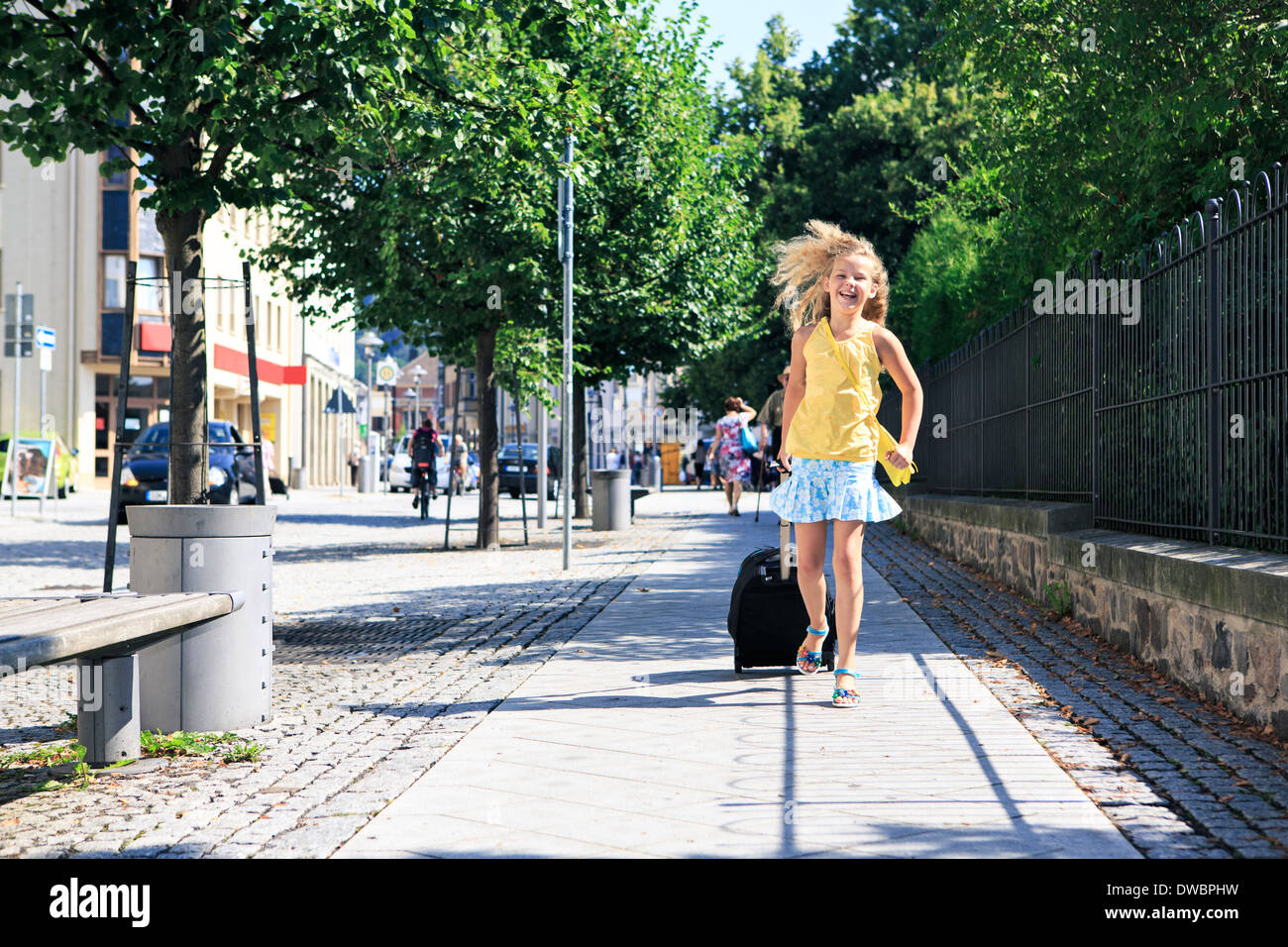 Girl with pulling suitcase running on sidewalk Stock Photo - Alamy