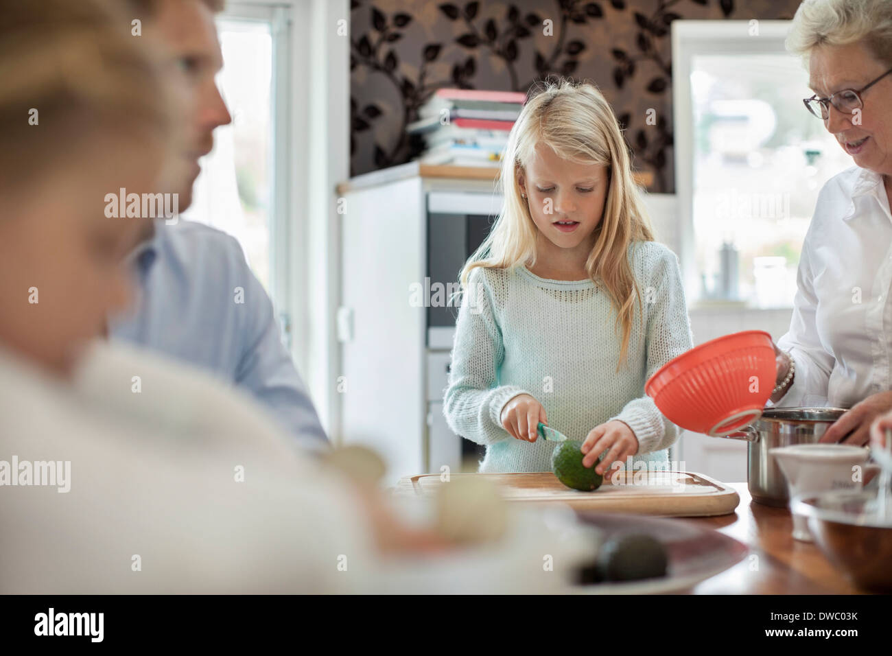 Girl cutting vegetables while cooking food with family in kitchen Stock ...