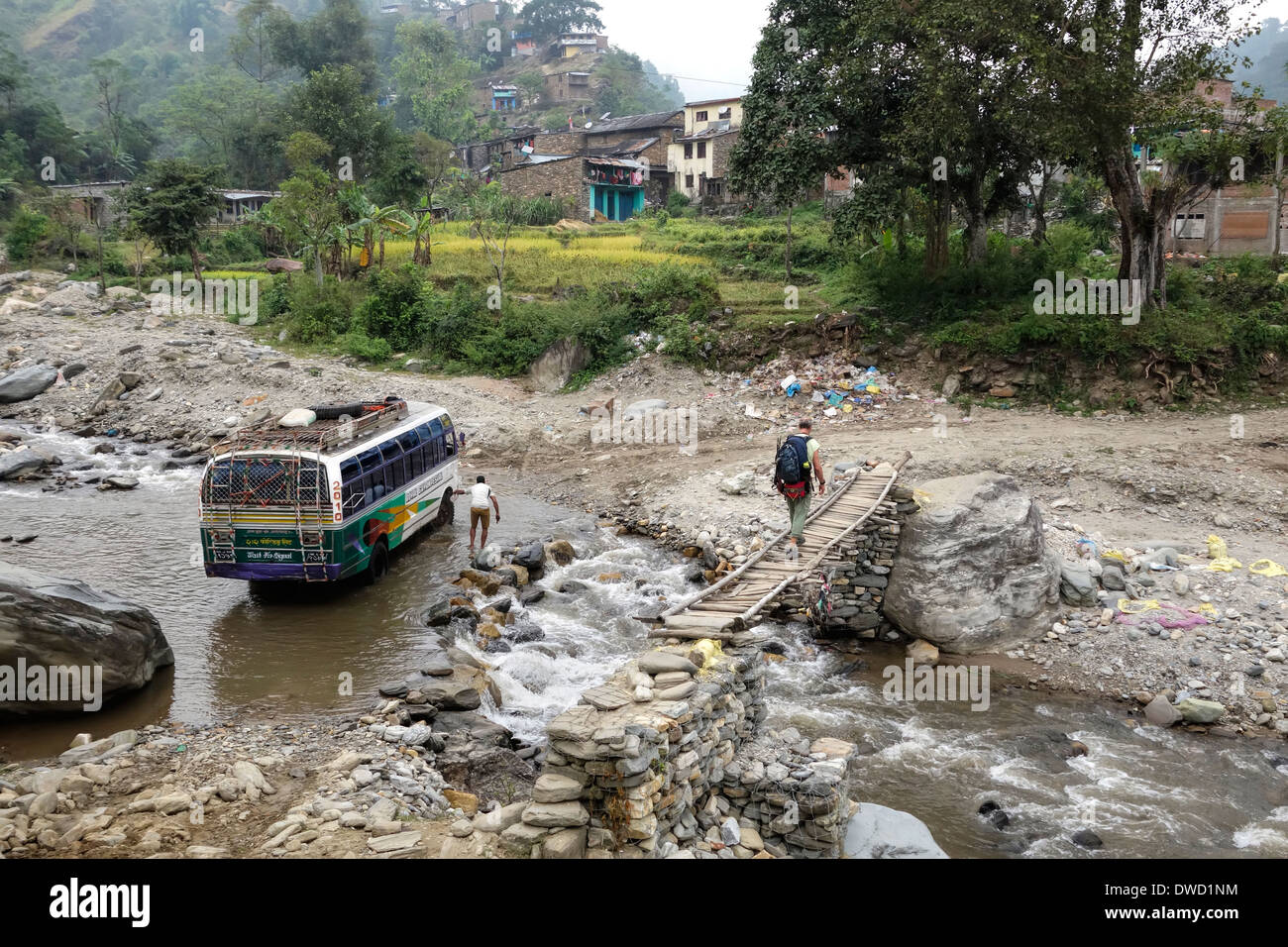 Trekker crossing a bridge over a stream where a driver is washing a bus ...