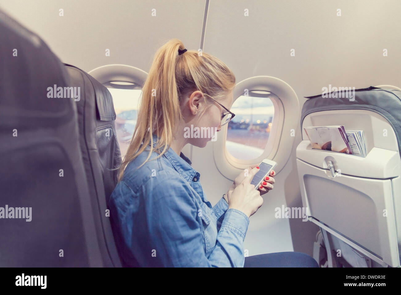 Blond young woman in airplane using smartphone Stock Photo - Alamy