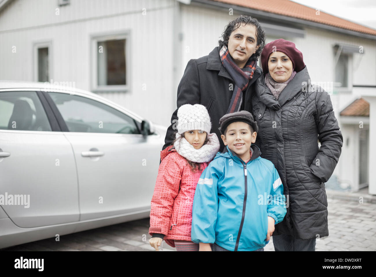 Portrait of happy Muslim family in warm clothing standing outside house ...