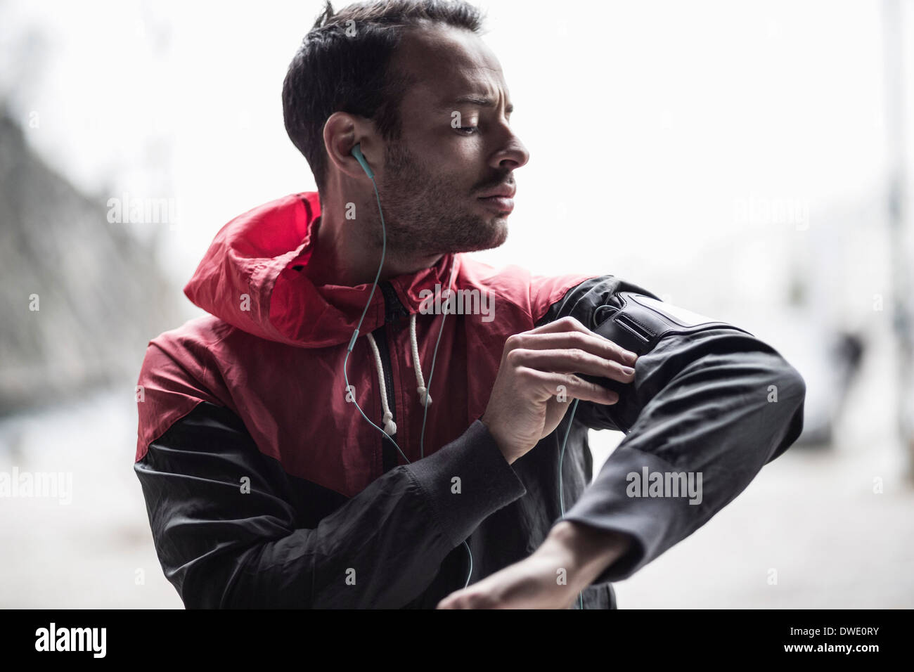 Sporty man adjusting arm band while listening to music Stock Photo - Alamy