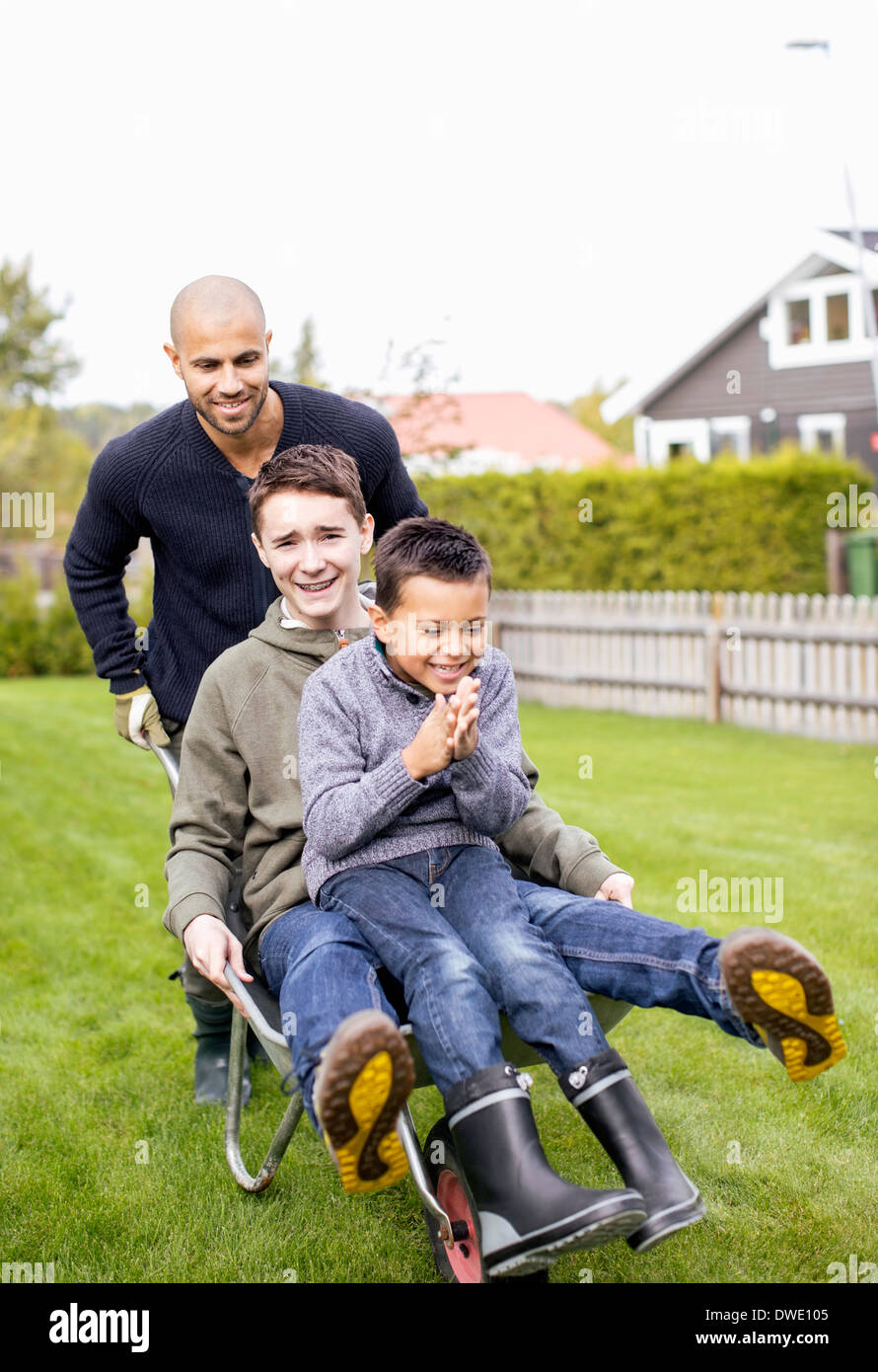 Father pushing children in wheel barrow at yard Stock Photo - Alamy