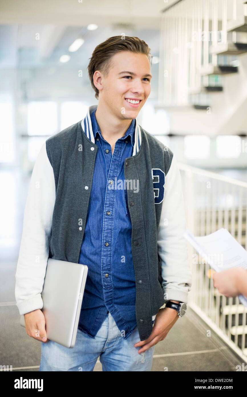Happy male university student with laptop in college corridor Stock ...