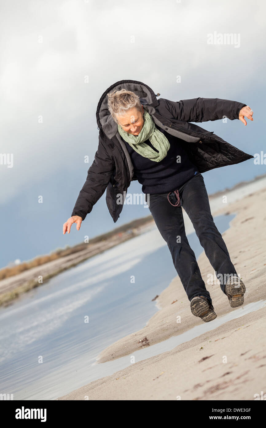 Happy senior woman frolicking on the beach striding along with ...