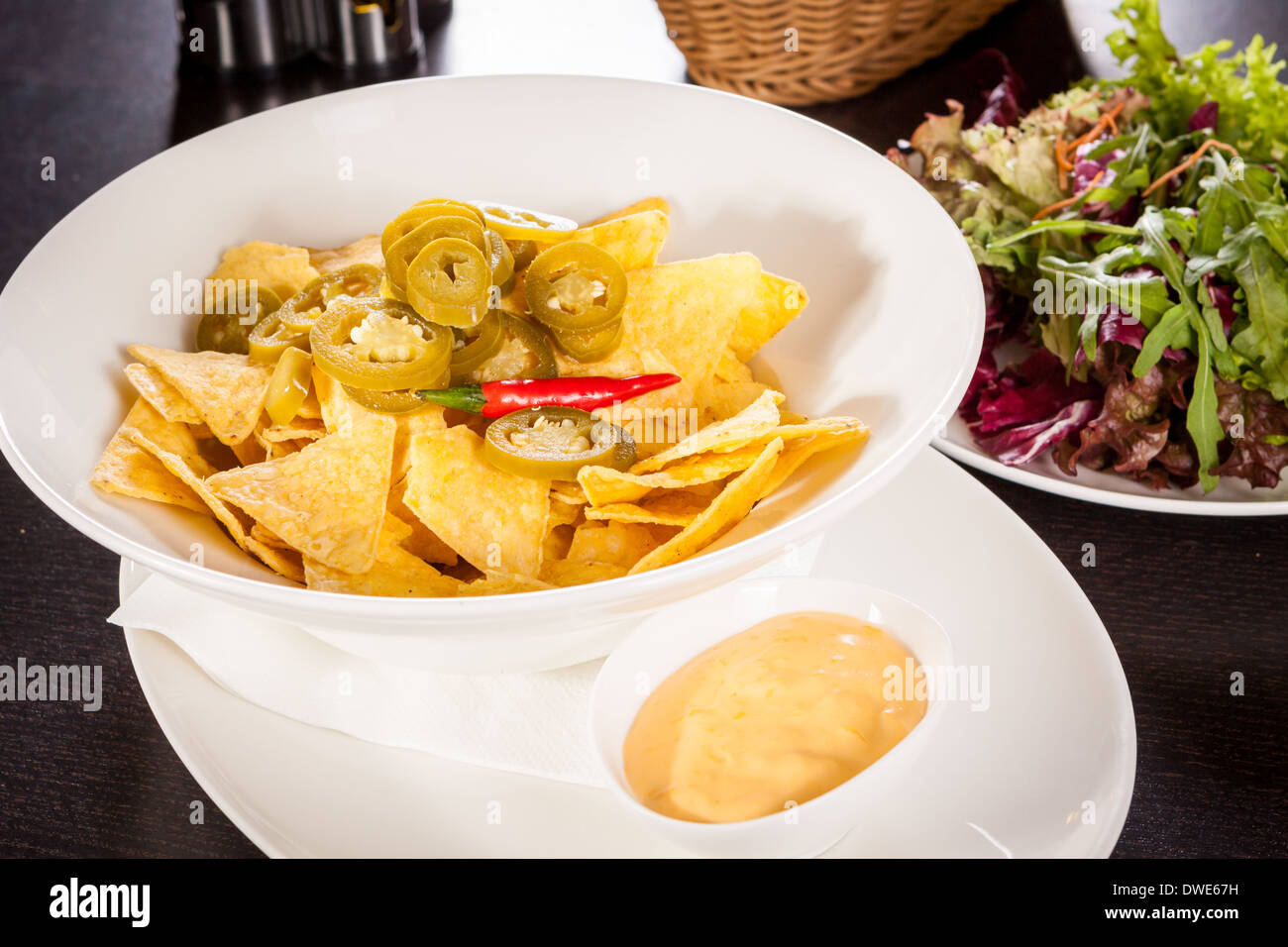 Bowl of crisp golden corn nachos with cheese sauce or dip and olives ...