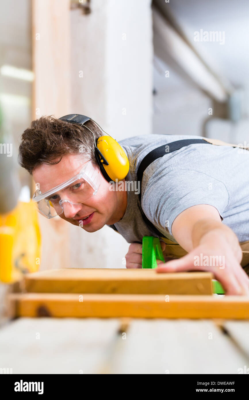 Carpenter working on an electric buzz saw cutting some boards, he is ...