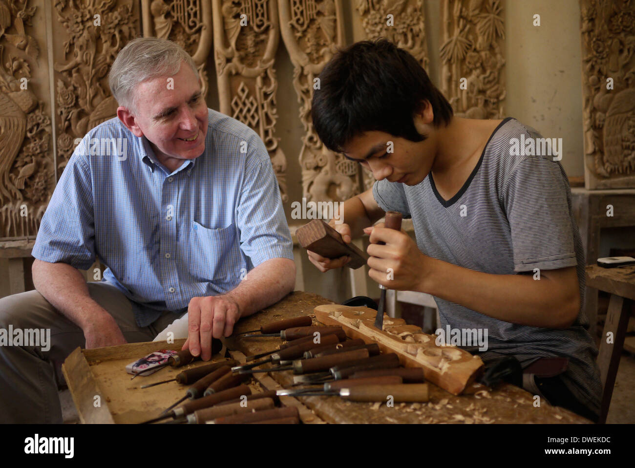 Vietnam, wood carver at work, watched by American Catholic missionary ...