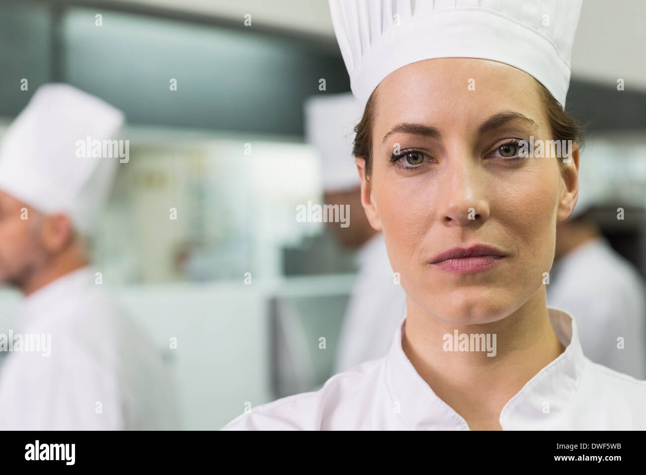 Serious chef looking at camera with team working behind Stock Photo - Alamy