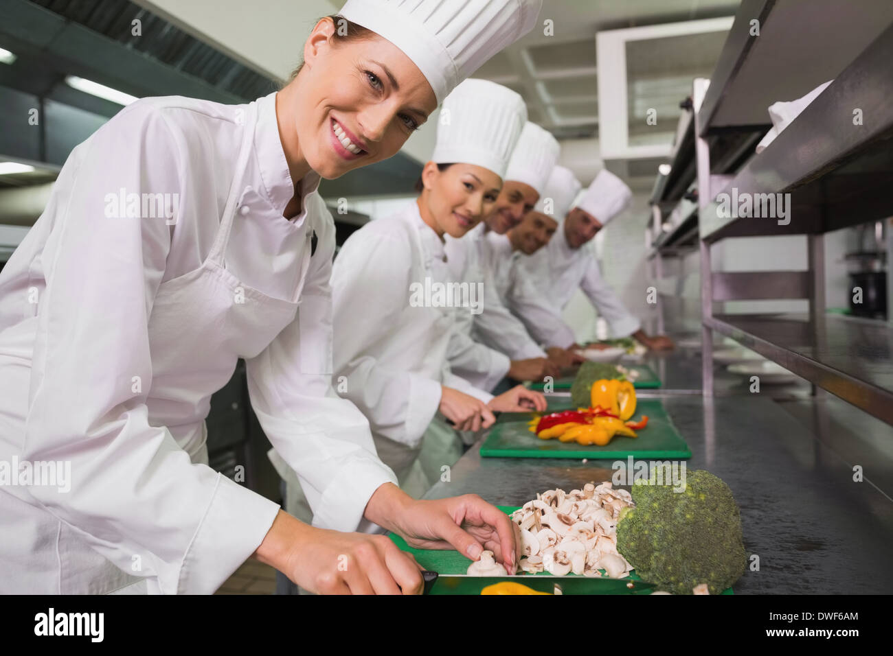 Row of happy trainee chefs slicing vegetables in a commercial kitchen ...