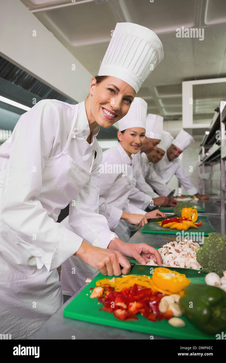 Row of happy trainee chefs slicing vegetables in a commercial kitchen ...