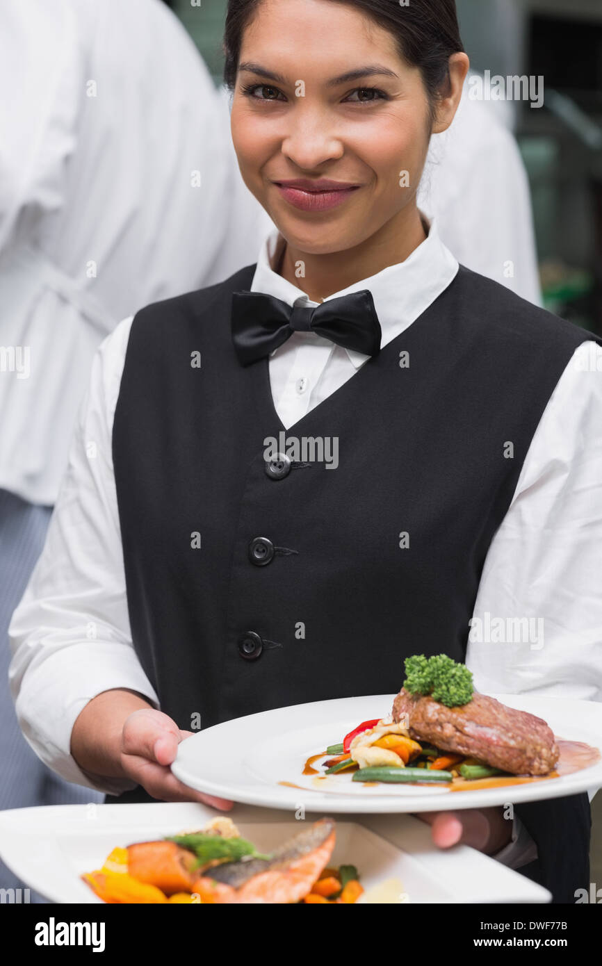 Happy waitress holding steak dinner and salmon dinner Stock Photo - Alamy