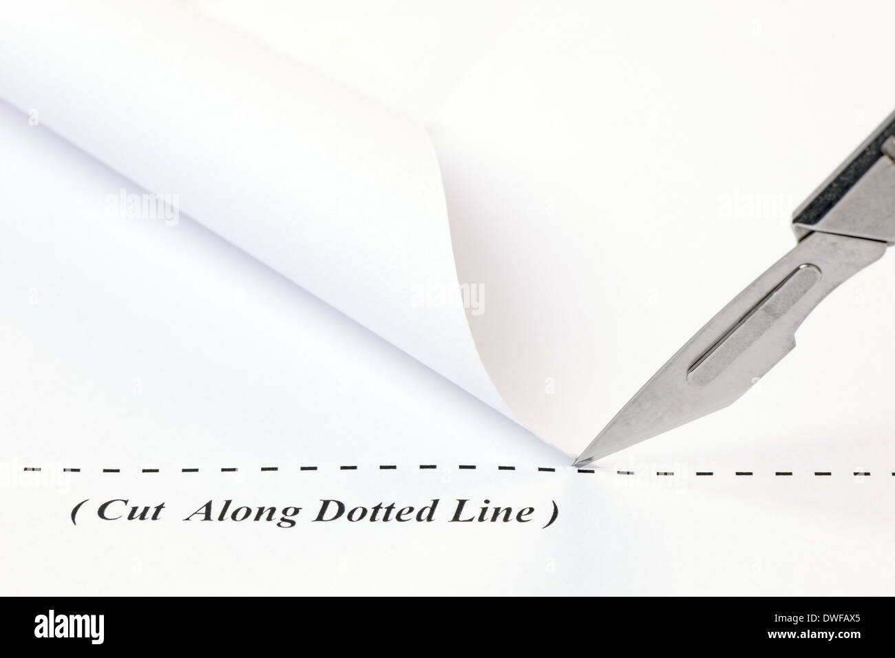 Close up of a scalpel cutting along a dotted line on a sheet of white ...