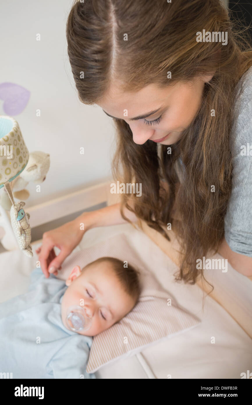 Happy mother watching over baby son sleeping in crib Stock Photo - Alamy
