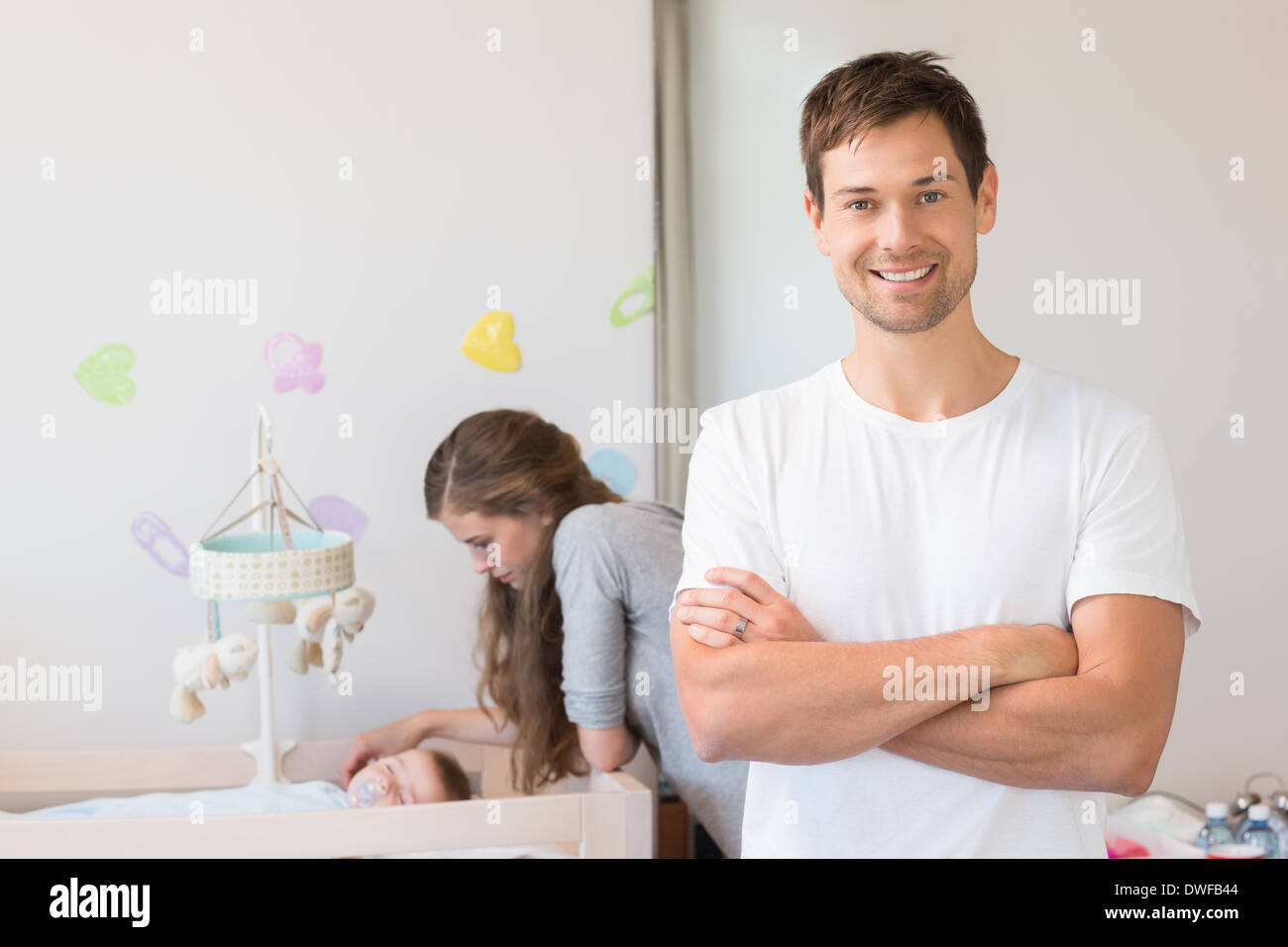 Happy mother watching over baby son in crib with father smiling at ...