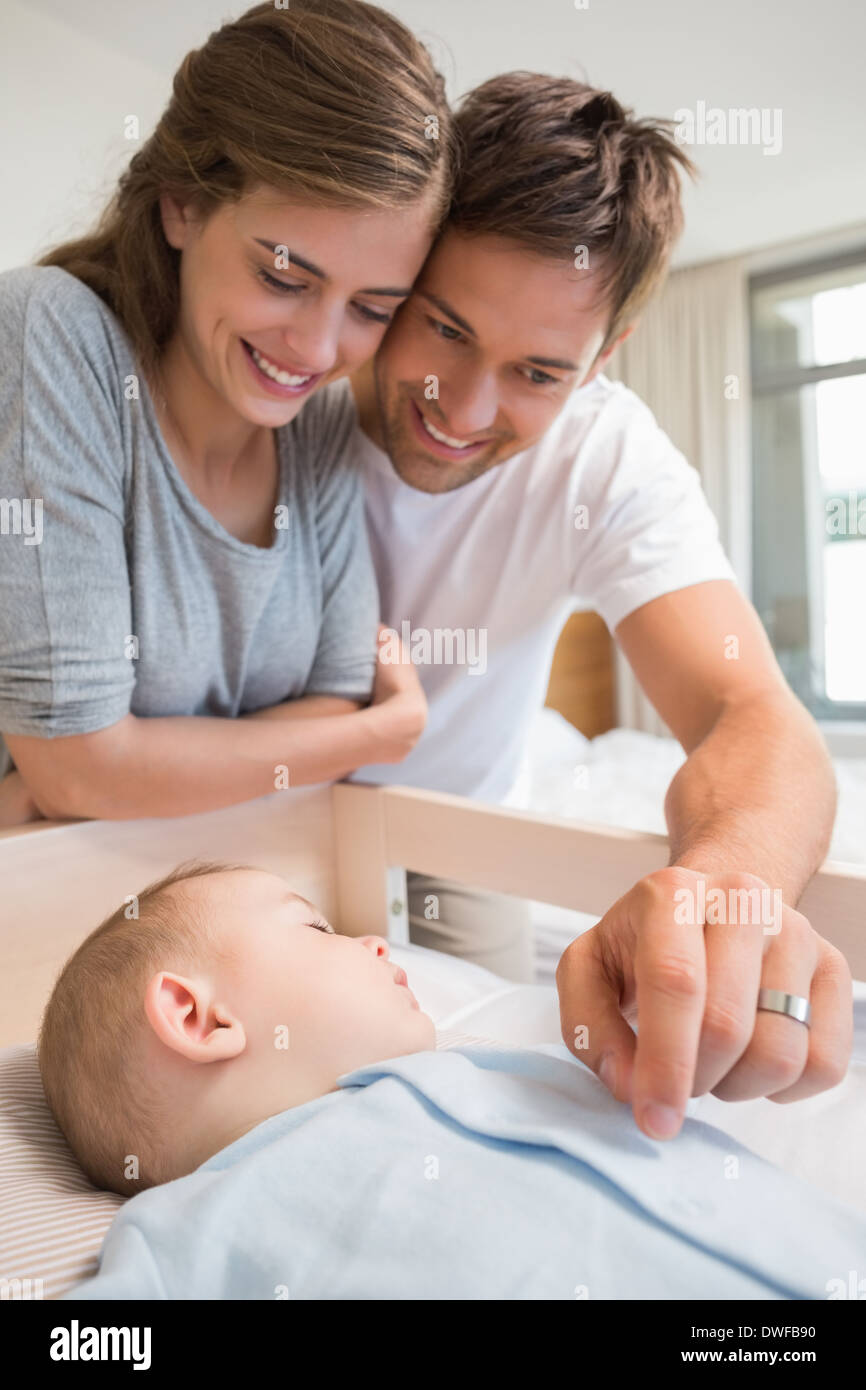 Happy parents watching over baby son sleeping in crib at home in ...