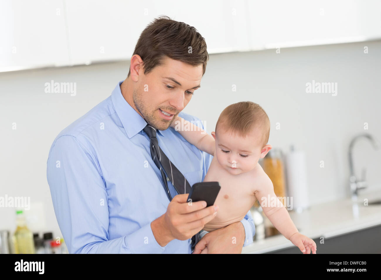 Busy father holding his baby son before work at home in the kitchen ...