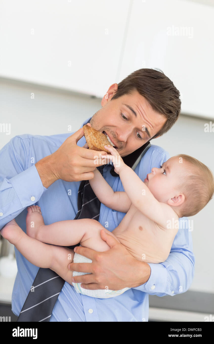 Busy father holding his baby son before work and eating toast Stock ...