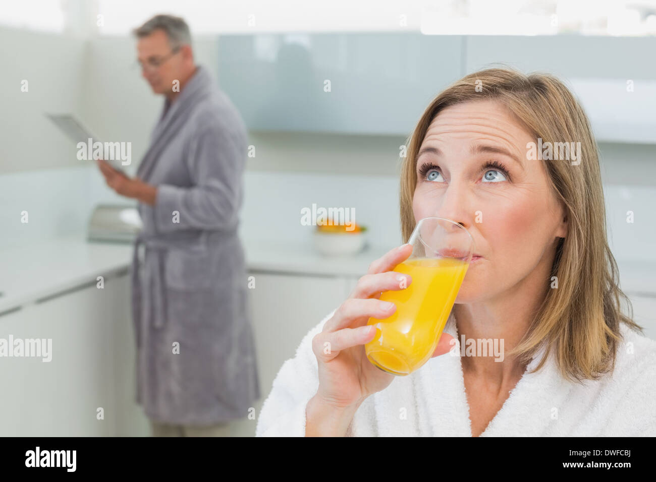 Woman drinking orange juice with man in background Stock Photo - Alamy